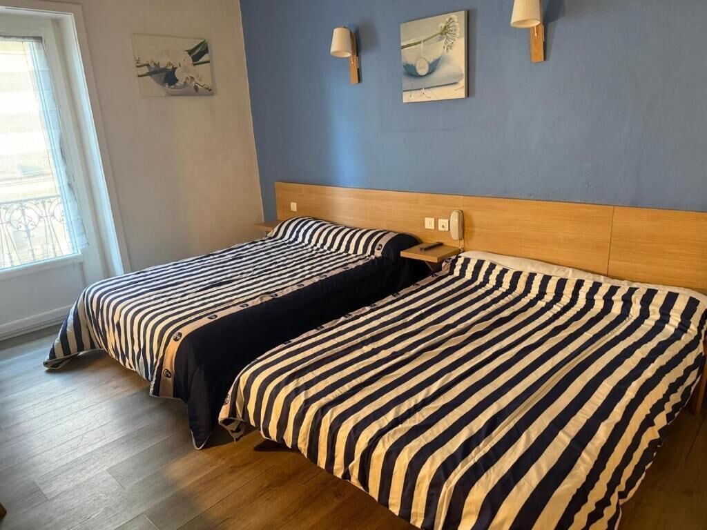 Quarto com duas camas, cabeceira de madeira, luminárias na parede e obras de arte.