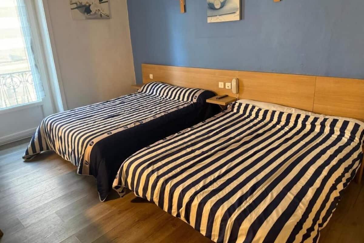 Quarto com duas camas, cabeceira de madeira, luminárias na parede e obras de arte.