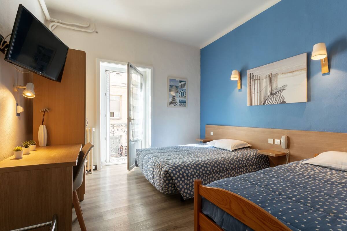 Quarto de hotel com escrivaninha, duas camas, televisão e um quadro na parede.