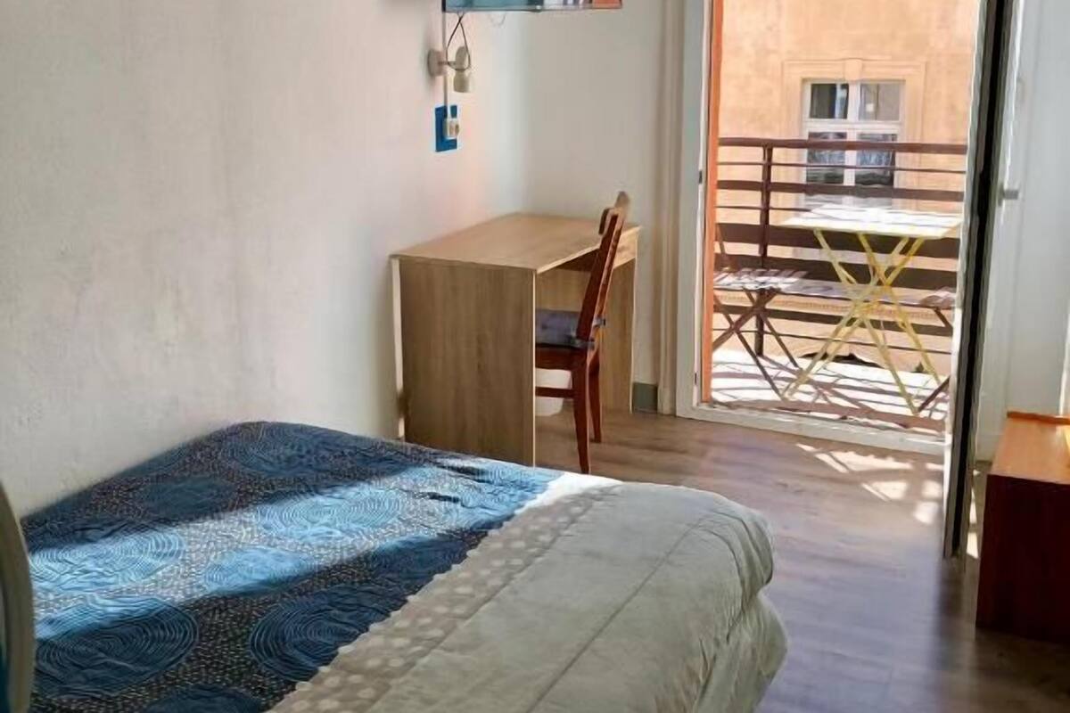 Quarto com cama, escrivaninha e cadeira. Varanda com mesa e cadeiras.