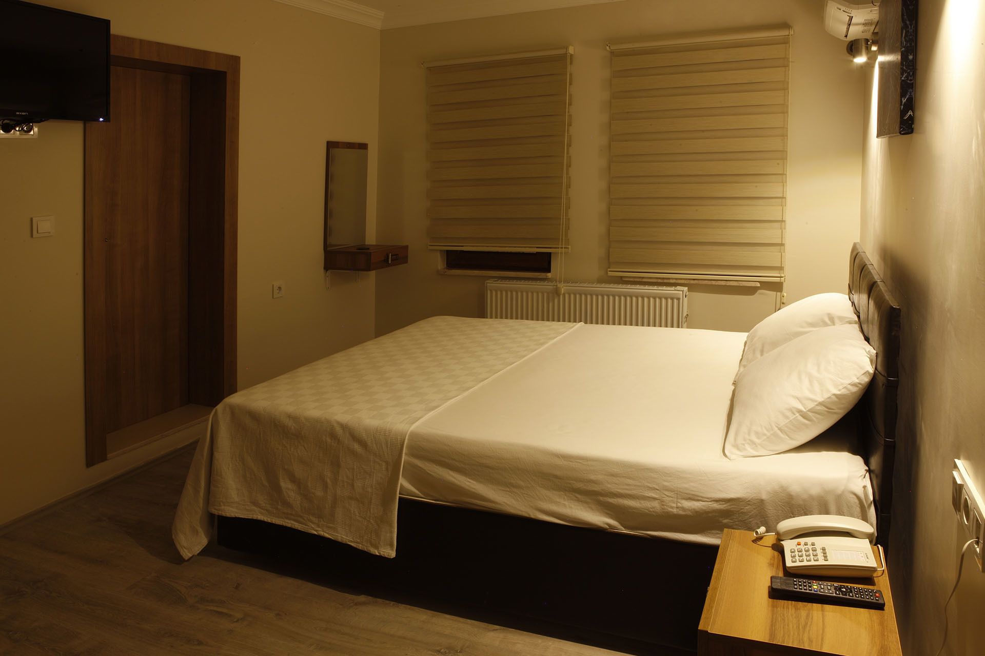 Quarto de hotel com cama, telefone ao lado da cama, controle remoto, espelho e radiador.