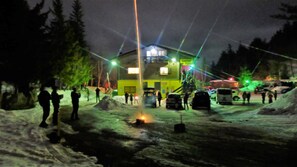 Um edifício com fachada amarela, rodeado de neve, com veículos de emergência e pessoas.