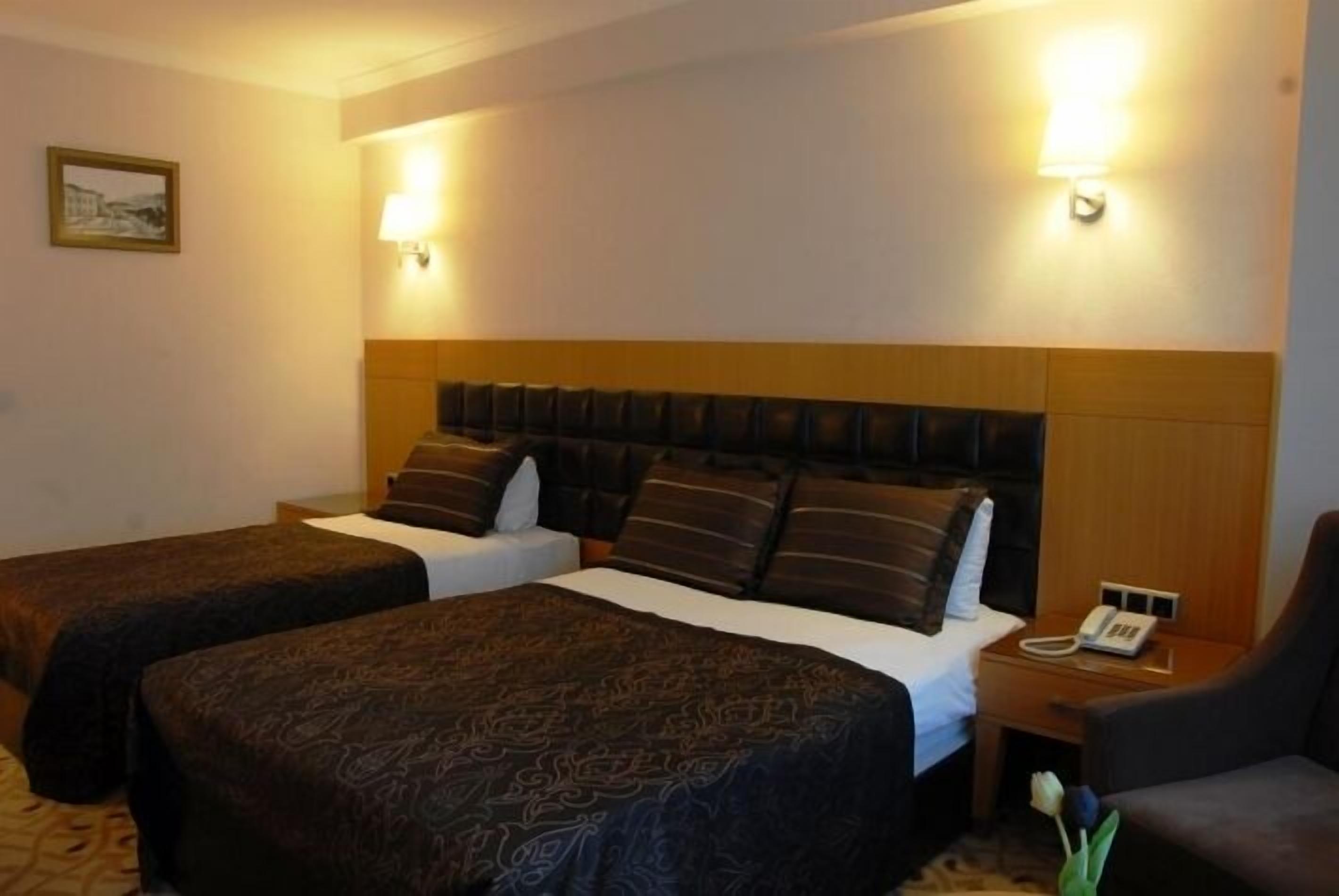Quarto de hotel com duas camas, cabeceira de madeira, abajures, um telefone e uma pequena mesa com um vaso de flores.
