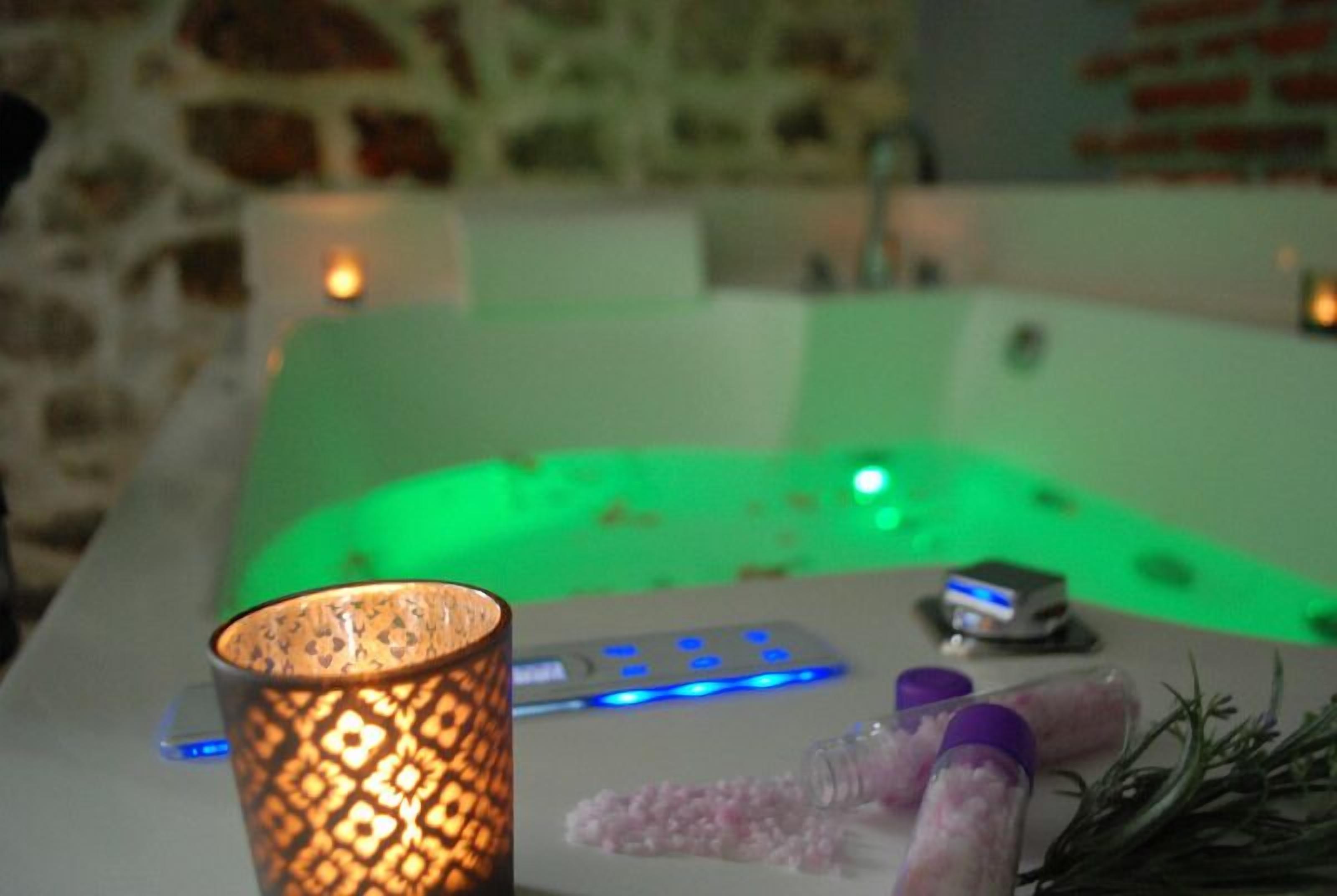 Uma área de spa com uma banheira iluminada em verde, uma vela e algumas ervas.