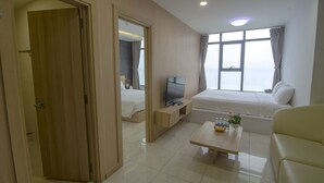 Quarto de hotel moderno com cama, televisão, sofá, mesa de centro e uma grande janela.
