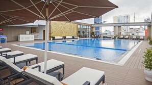 Uma área de piscina no terraço com espreguiçadeiras, guarda-sóis, um bar e vista para o horizonte da cidade.