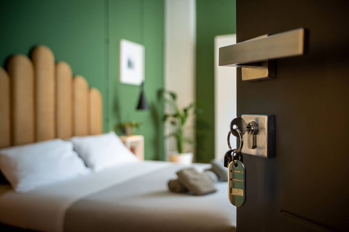 Uma cama com roupa de cama branca, cabeceira de madeira e mesa de cabeceira com abajur.