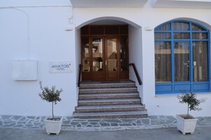 Entrada de hotel com porta de madeira, escada e duas plantas em vasos.
