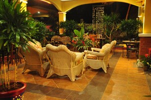 Um pátio interno bem iluminado, com móveis de vime, plantas em vasos e chão de azulejos.