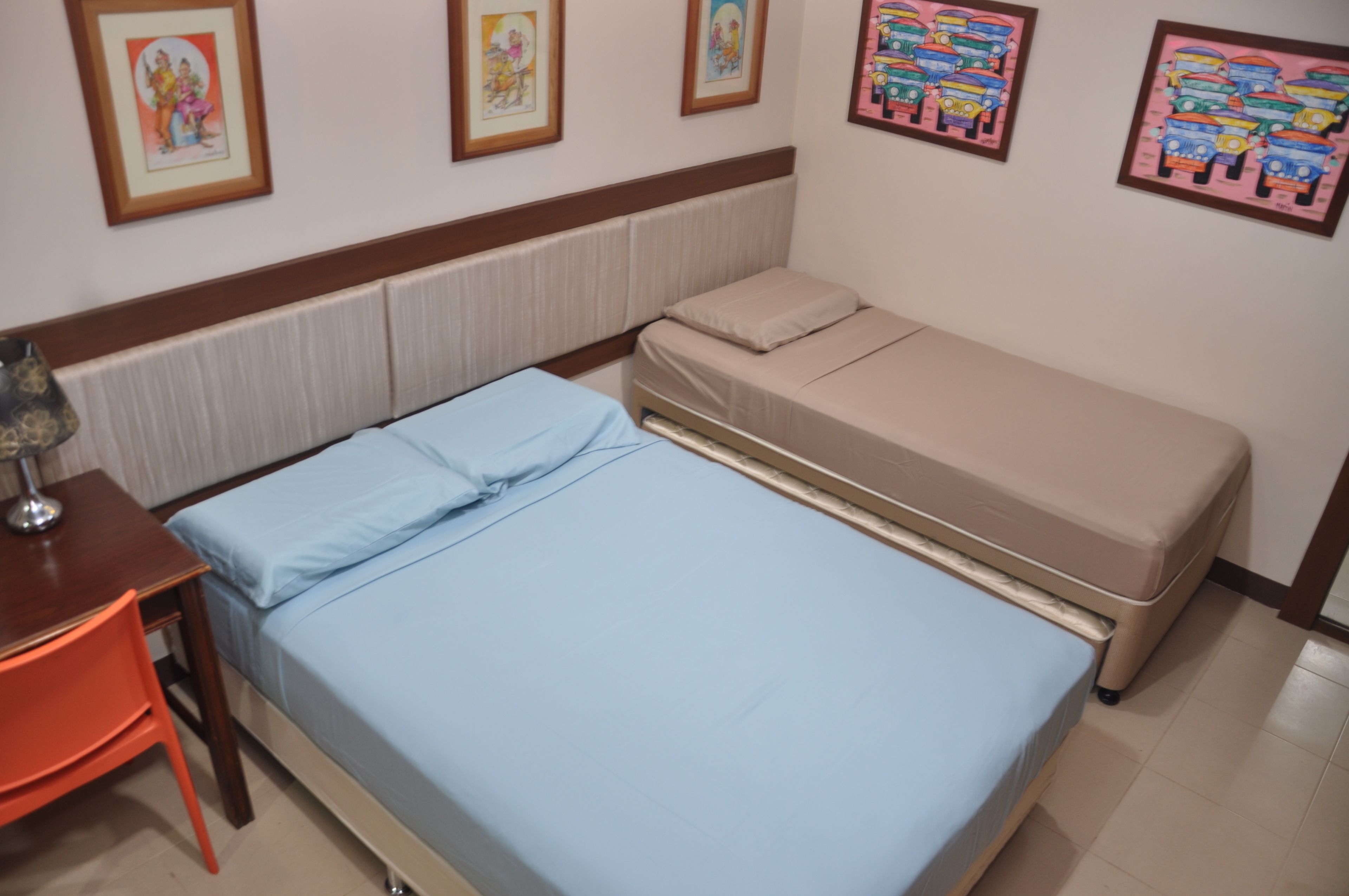 Uma cama de solteiro com um colchão azul e um bege sobre uma estrutura de madeira. Há uma pequena mesa com um abajur ao lado da cama.
