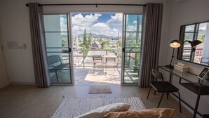 Quarto com uma grande porta de correr de vidro que dá para um espaço de pátio ao ar livre. Há uma mesa com cadeira, uma luminária e uma pequena mesa com uma planta.