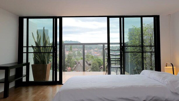 Quarto com uma janela grande, uma cama, um banco e uma planta em vaso.