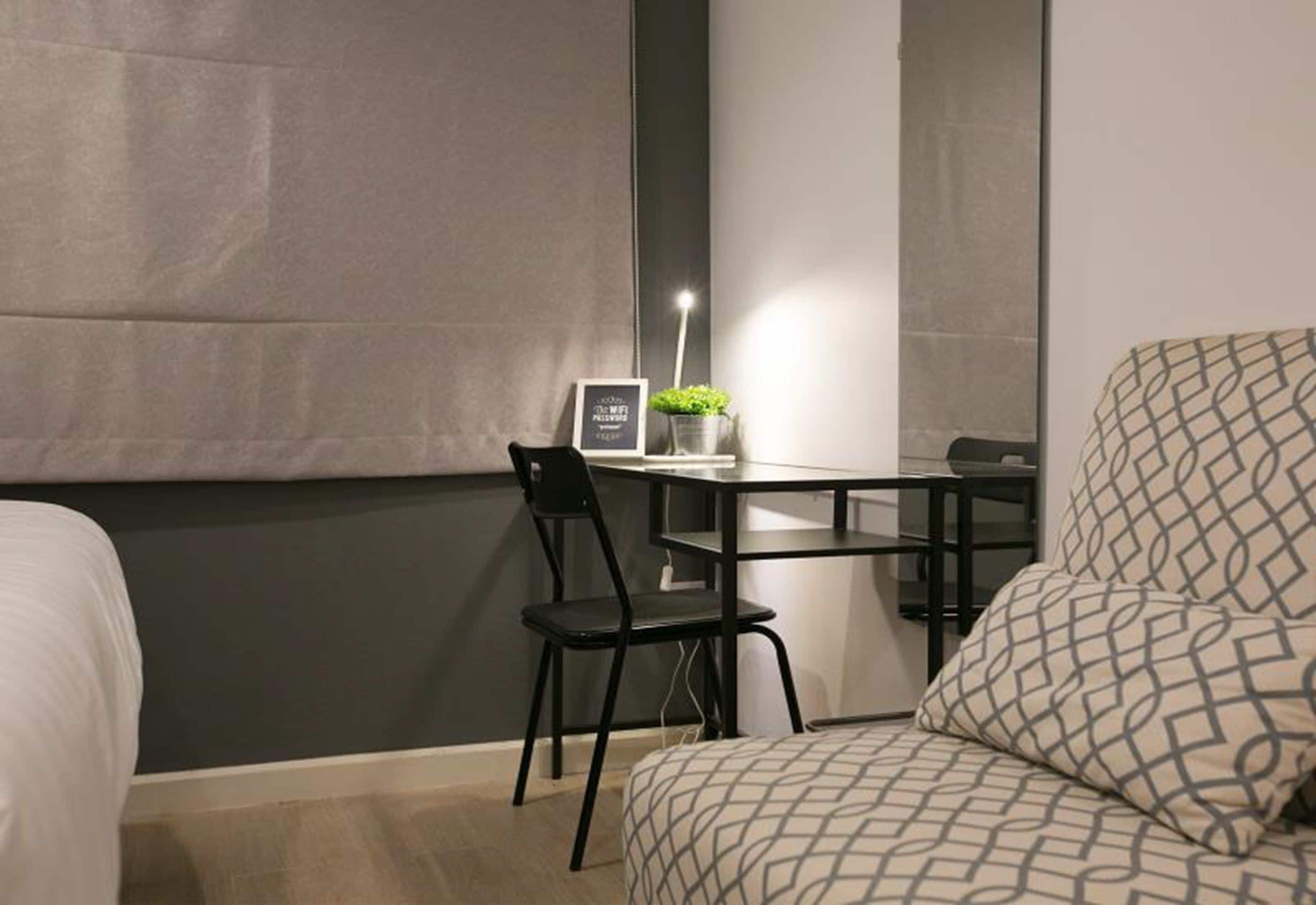 Quarto com uma cama, uma escrivaninha com cadeira, um espelho e uma pequena planta em vaso.