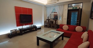 Sala de estar com sofá vermelho, mesa de centro de vidro, TV de tela plana montada em um painel vermelho e porta com painel de vidro azul.