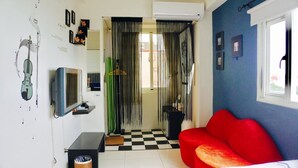Quarto compacto com um sofá vermelho, uma mesa pequena, uma televisão e piso xadrez.