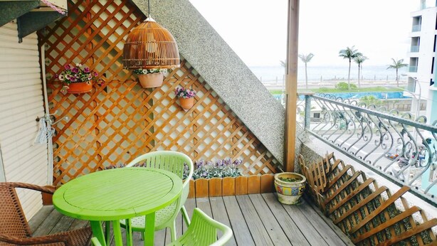 Uma varanda com mesa e cadeiras verdes, plantas em vasos e vista para a praia.