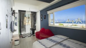 Quarto de hotel moderno com uma grande janela que oferece vista para a praia e para o oceano.
