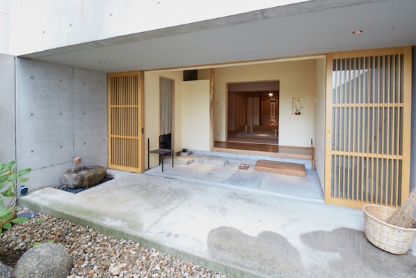 Uma entrada tradicional japonesa com um caminho de concreto que leva a uma porta de madeira.