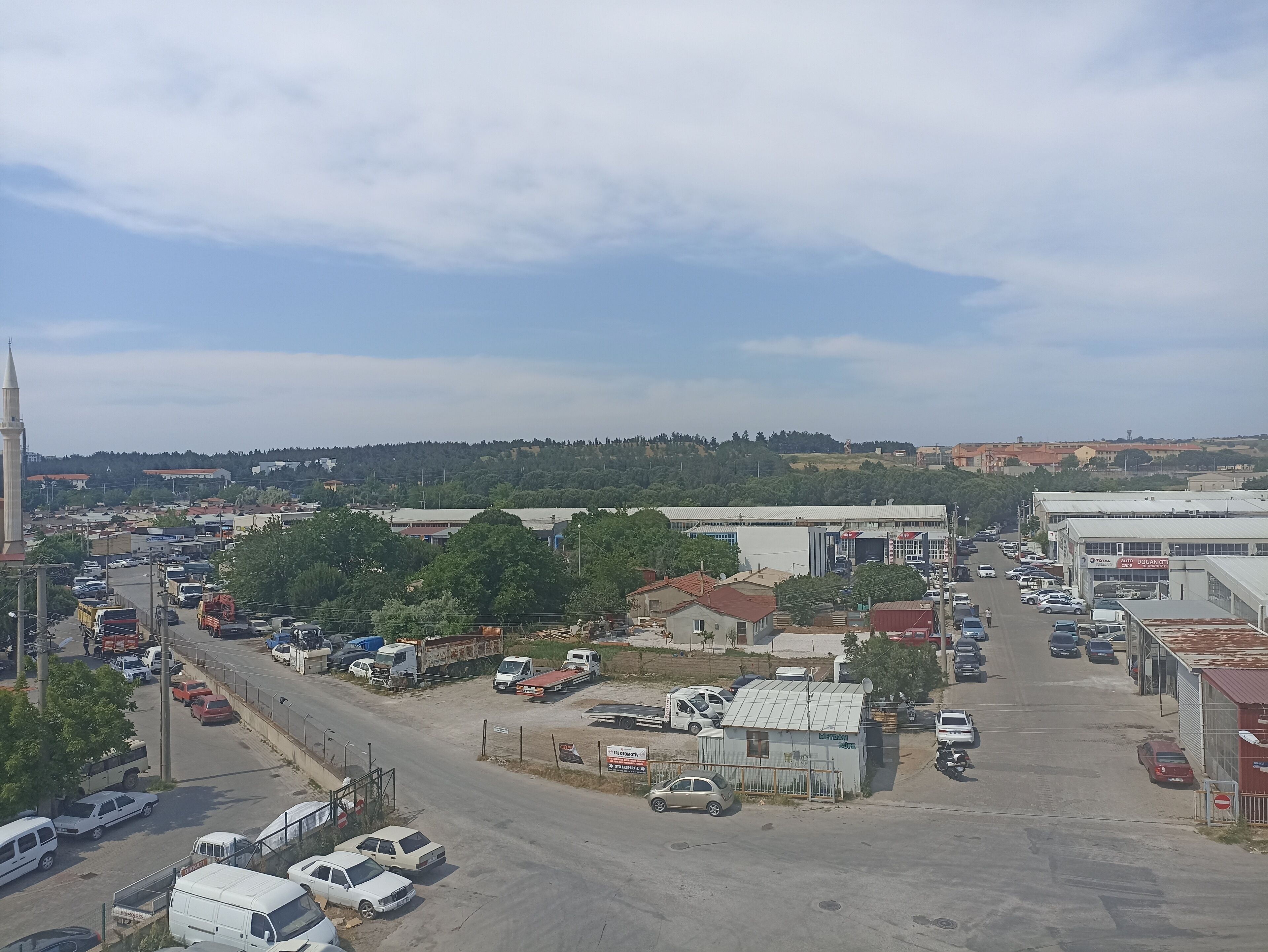 Uma extensa área industrial com vários edifícios, veículos estacionados e uma mesquita com um minarete.