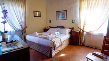 Cama bem arrumada com um laptop, mesa de cabeceira com abajur e janela com cortinas.