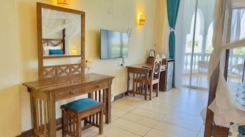 Um quarto com escrivaninha de madeira, uma cadeira, televisão e varanda com cortinas.