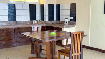 Uma cozinha com mesa, cadeiras, armários e bancada.