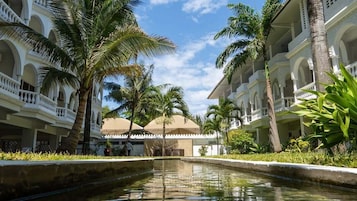Pátio de hotel com fonte central, palmeiras e edifícios com varandas.