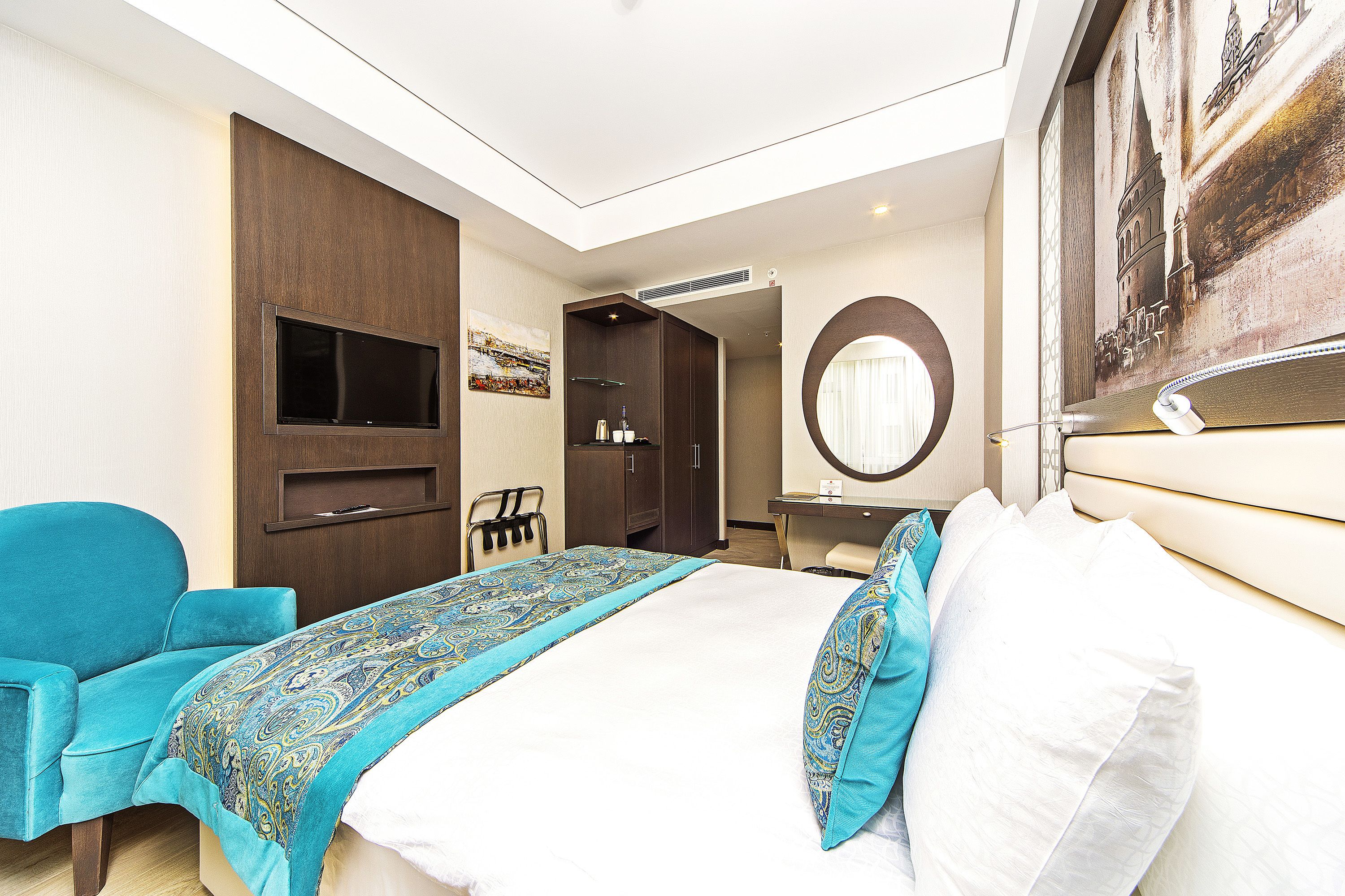 Quarto de hotel com cama, escrivaninha, cadeira, televisão e um quadro na parede.