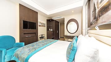 Quarto de hotel com cama, escrivaninha, cadeira, televisão e um quadro na parede.