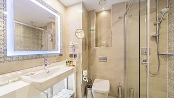 Uma casa de banho moderna com cabine de duche em vidro, um espelho grande e lavatório com produtos de higiene pessoal.