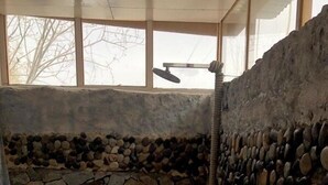 Casa de banho com parede de pedra, chuveiro e uma pequena janela.