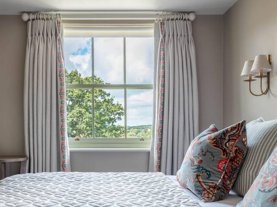 Quarto com uma cama grande, janela com cortinas e vista para árvores.