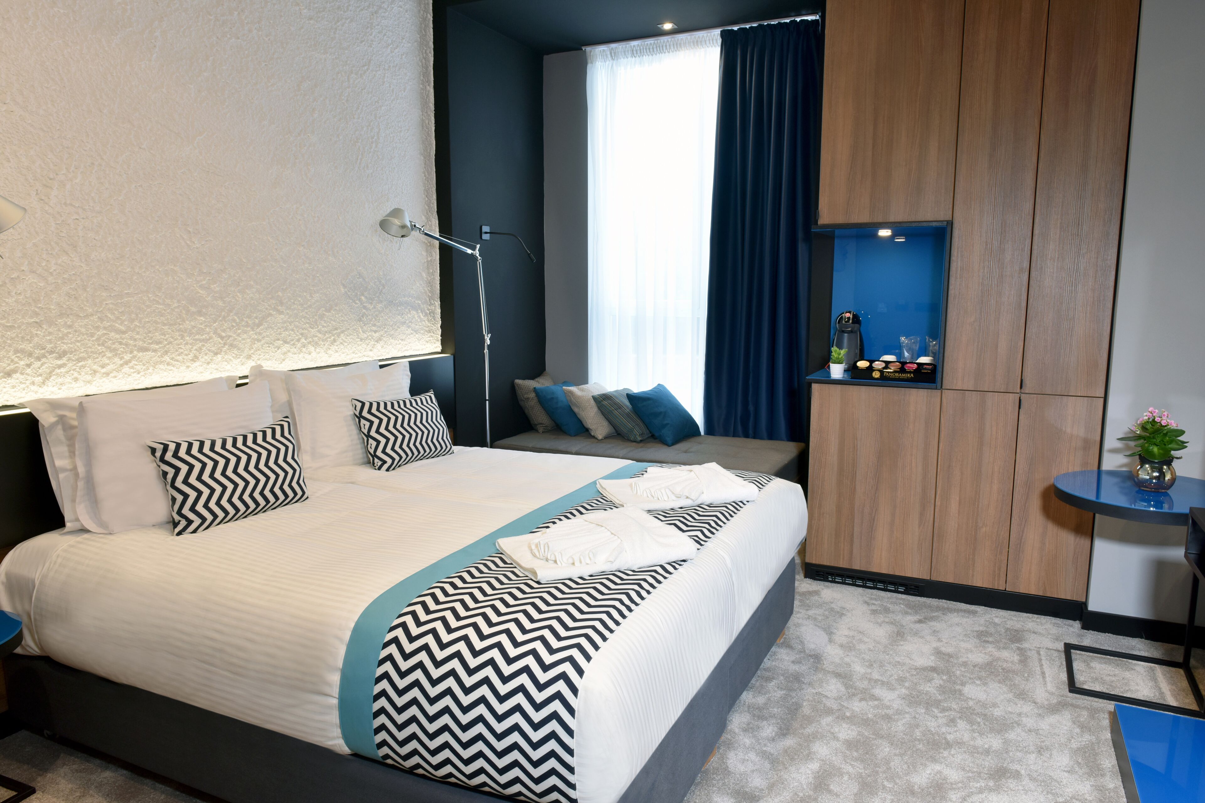 Quarto de hotel moderno com uma cama grande, mesa de cabeceira, escrivaninha e armário.