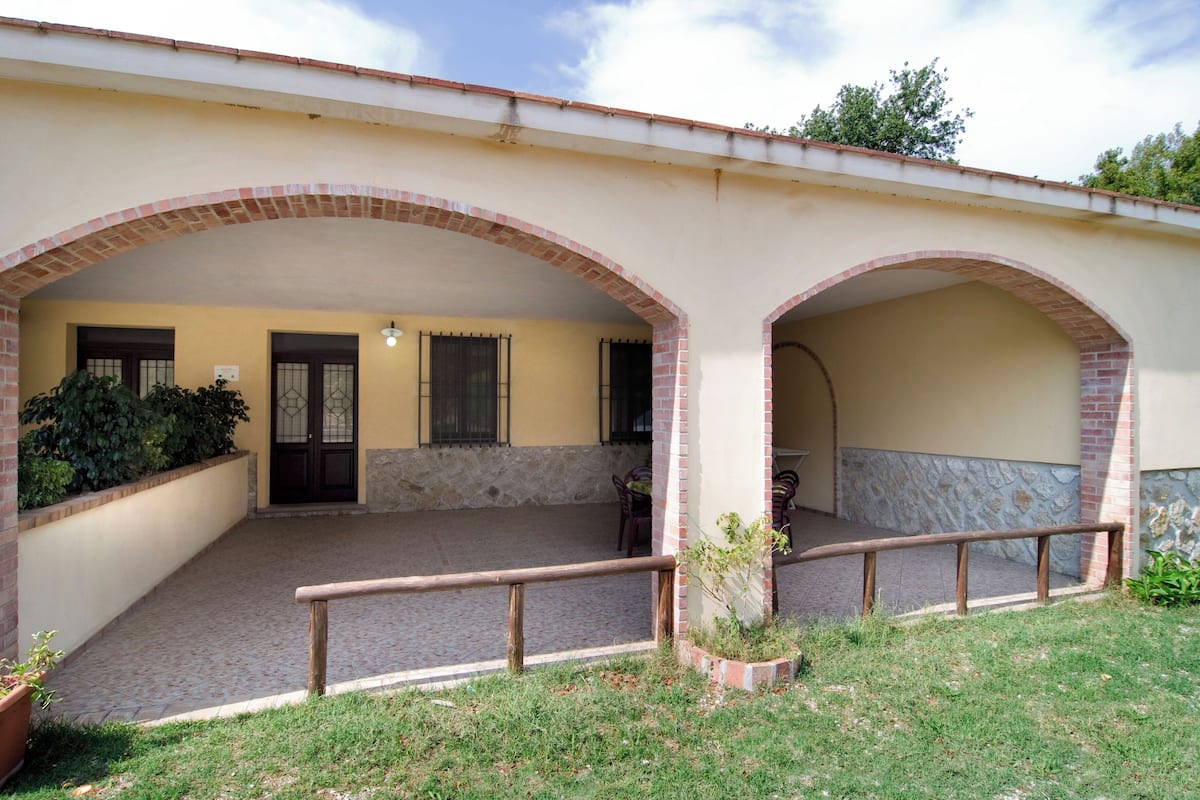 Um edifício com duas entradas em arco, um pátio pavimentado e uma pequena área de estar.