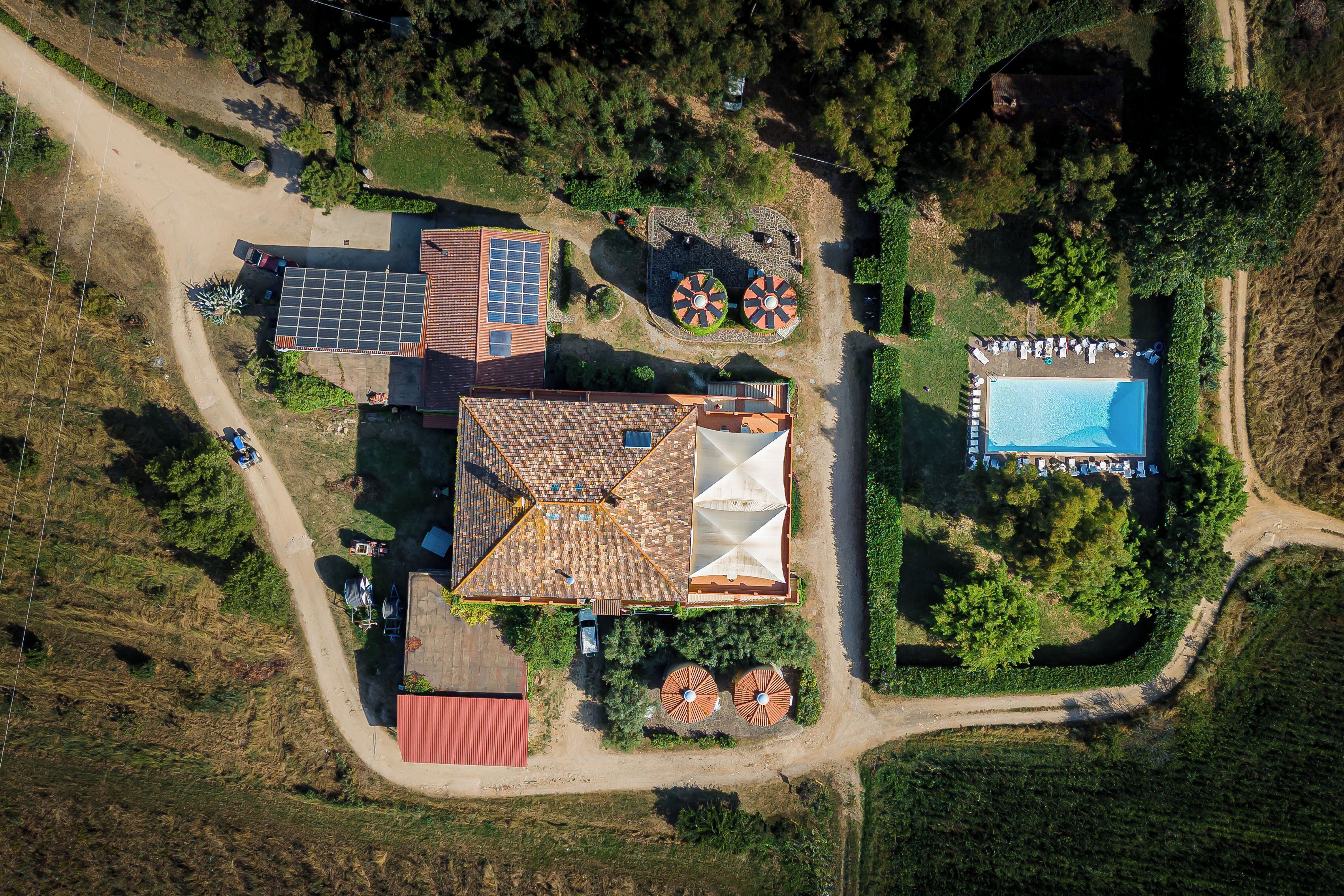 Vista aérea de uma propriedade com piscina, painéis solares e um edifício grande com telhado inclinado.