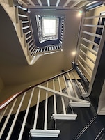 Escada com corrimão, piso preto e luminária acima.