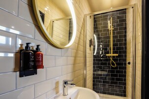 Casa de banho com lavatório branco, espelho e chuveiro com parede revestida a mosaico preto.