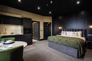 Quarto de hotel moderno com cama, área de refeições e cozinha compacta.