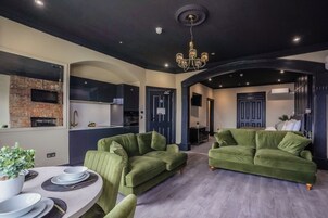 Uma sala de estar moderna com sofás verdes, uma mesa de jantar com pratos e uma área de cozinha com armários escuros.