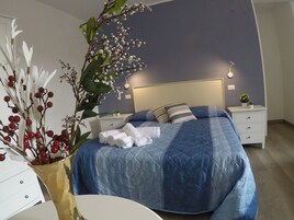 Quarto com cama, mesas de cabeceira, um vaso com flores e uma cômoda branca.