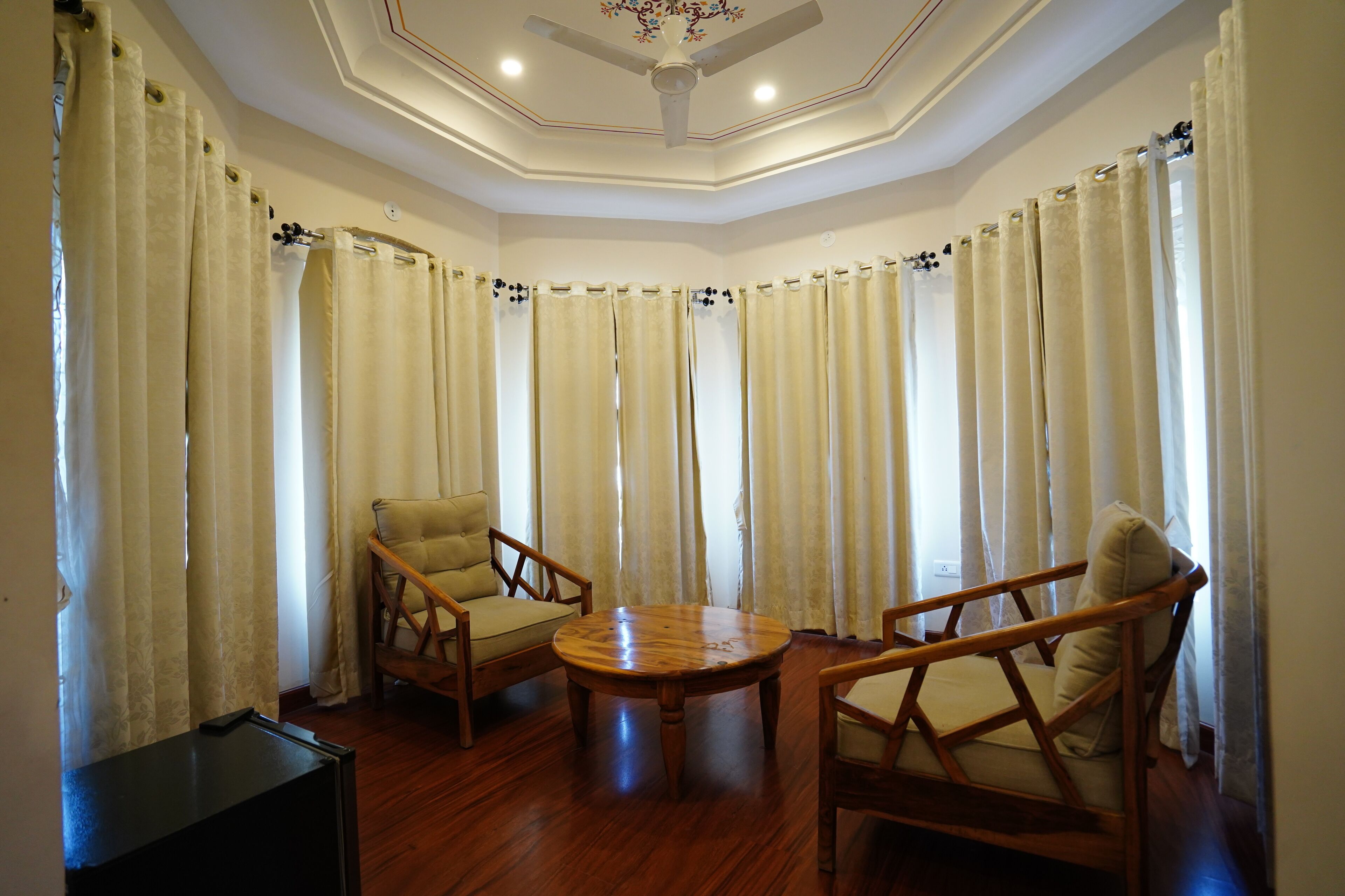 Um quarto com uma mesa redonda de madeira, duas poltronas de madeira e um ventilador de teto.