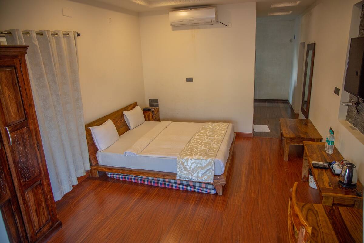 Quarto com cama de madeira, escrivaninha de madeira, espelho e ar condicionado.
