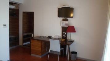 Quarto pequeno e moderno, com uma escrivaninha, cadeira e televisão na parede.