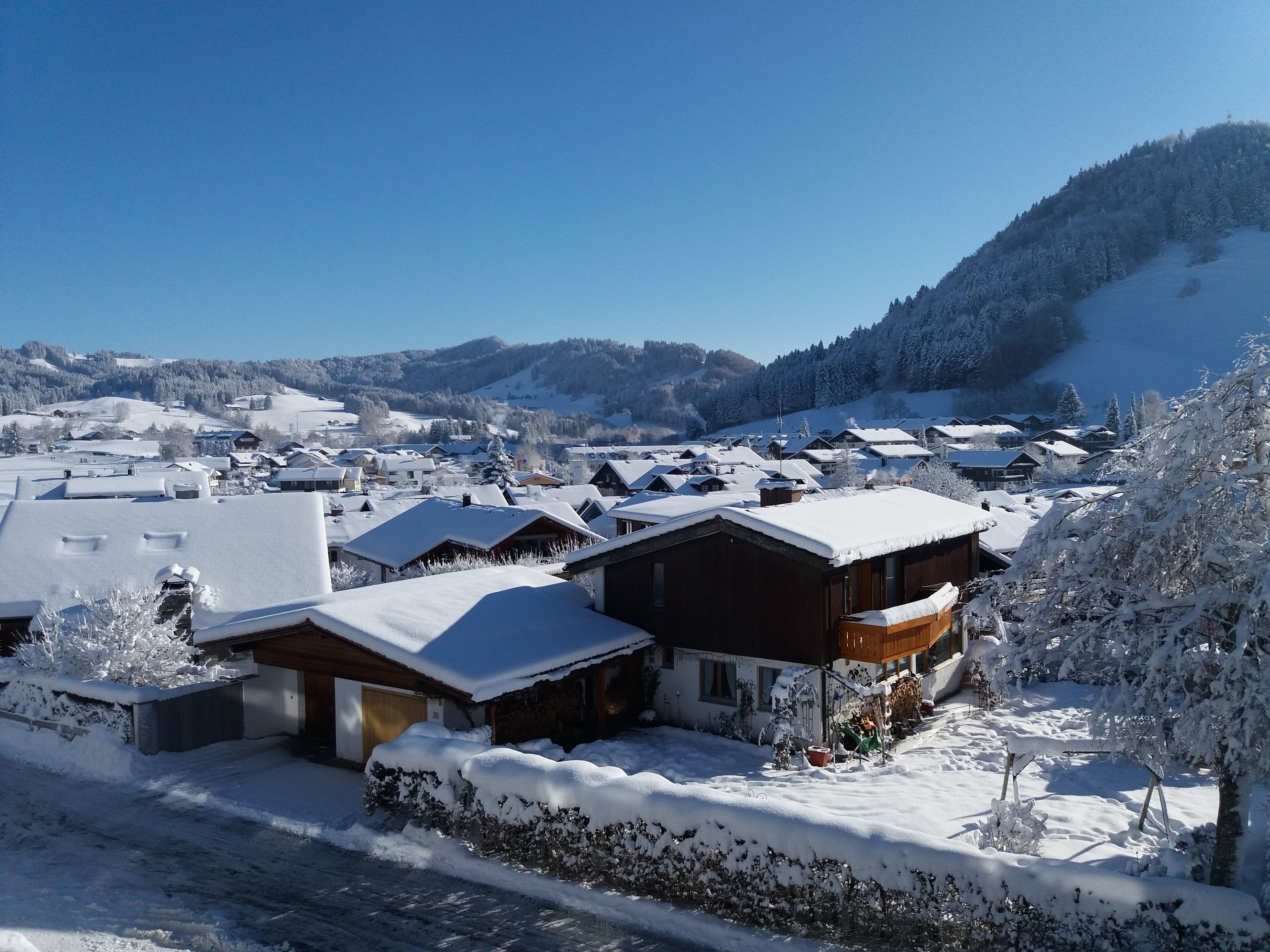 Vila coberta de neve com casas de madeira e montanhas ao fundo.