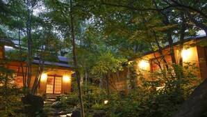 Um jardim japonês tradicional com caminhos de pedra, bambu e um edifício com iluminação quente.
