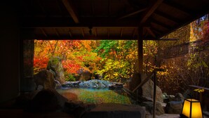 Uma onsen japonesa tradicional com vista para a folhagem de outono, um deck de madeira e um lanterneiro.