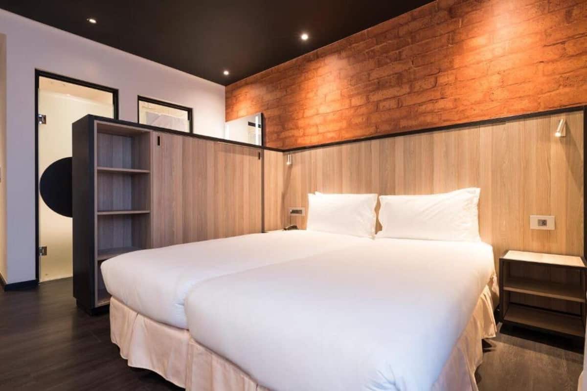 Quarto de hotel moderno com uma cama grande, painéis de madeira nas paredes e um guarda-roupa embutido.