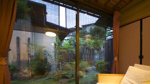 Quarto com porta de vidro deslizante que dá para um jardim com pequeno lago, bambu e cerca de madeira.
