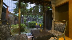 Quarto com vista para um jardim, uma mesa com um vaso de flores e duas cadeiras.