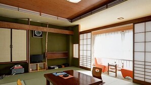Um quarto japonês tradicional com tatames, uma mesa de madeira baixa, uma televisão e portas deslizantes.